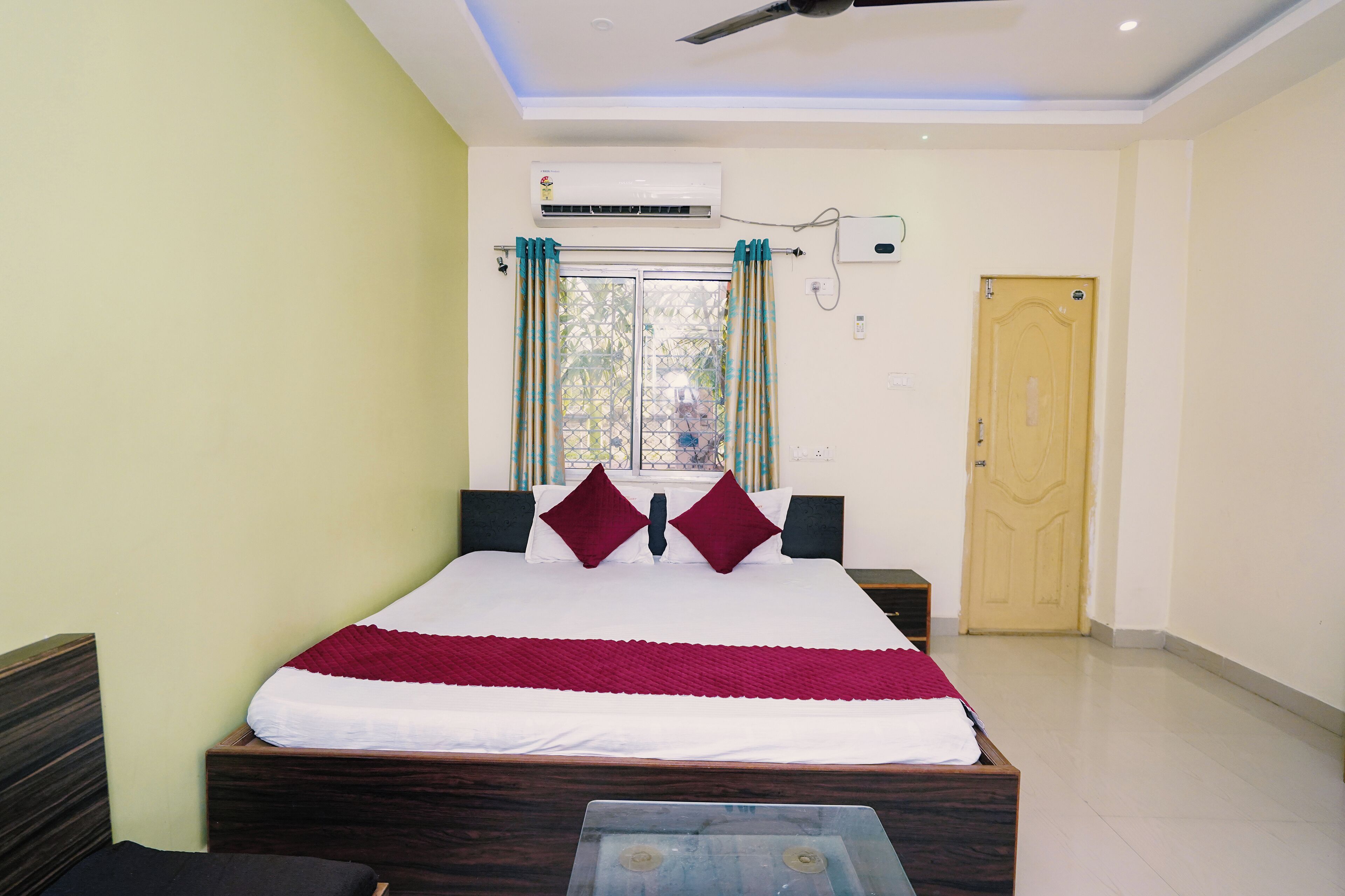 Quarto bem arrumado com cama, mesas de cabeceira, ventoinha no teto, ar condicionado e janela com cortinas.