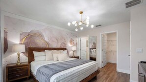 Quarto com cama de madeira, duas mesas de cabeceira com luminárias, um grande mural abstrato na parede e um closet espaçoso.