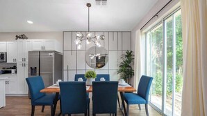 Uma cozinha moderna com armários brancos, uma geladeira de aço inoxidável e uma área de jantar com cadeiras azuis e uma mesa de madeira.