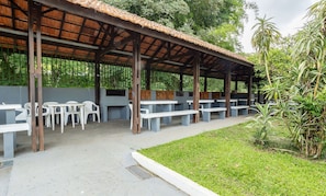 Uma área coberta ao ar livre com mesas e cadeiras, rodeada por vegetação.