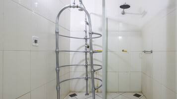 Chuveiro com estrutura metálica cromada, paredes revestidas de azulejo branco e ralo no chão.