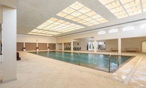 Piscina interna com água cristalina, chão em mosaico e teto com claraboias.