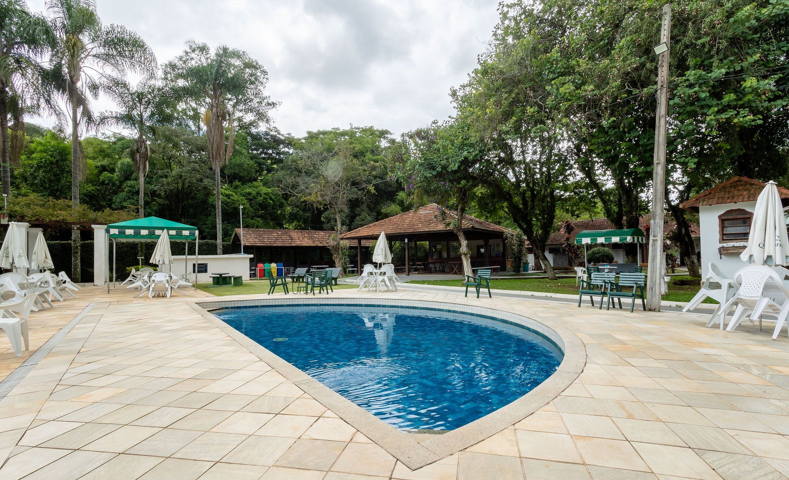 Piscina cercada por áreas de estar ao ar livre com guarda-sóis, um espaço coberto para relaxar e um edifício com telhado telhado.