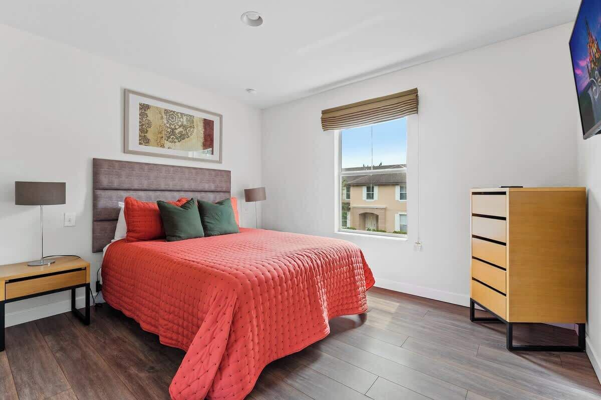 Quarto com uma cama grande, mesa de cabeceira, cômoda, janela com persianas e um quadro na parede.