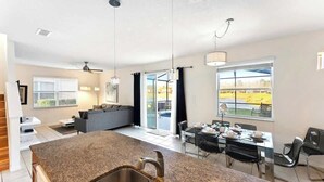 Cozinha moderna com bancadas de granito, pias de aço inoxidável e área de refeições com mesa e cadeiras de vidro.