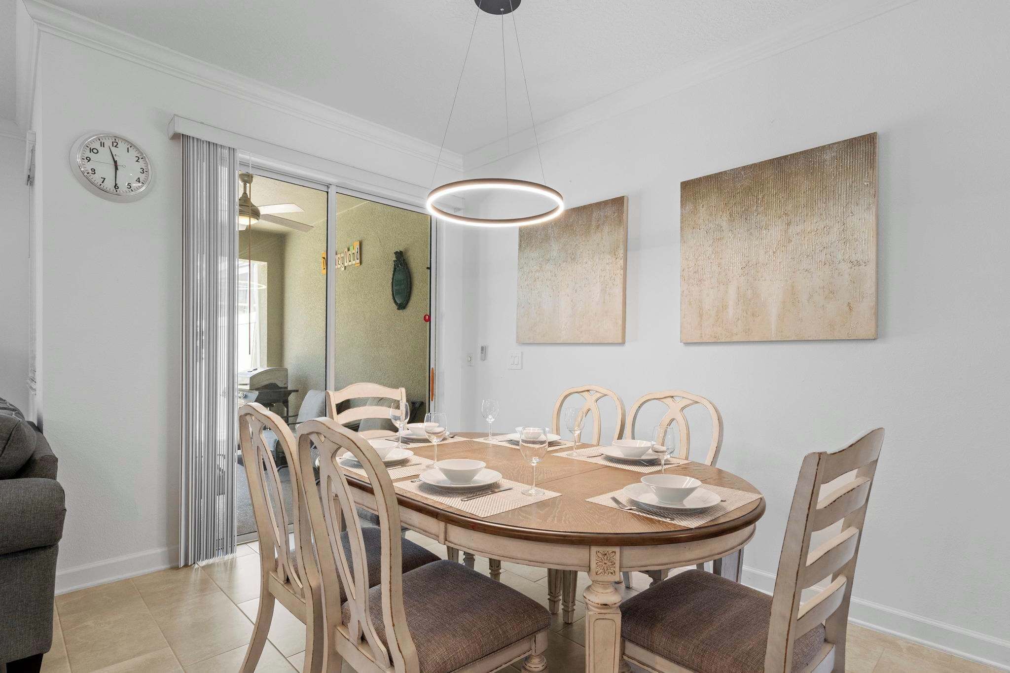 Uma sala de jantar com uma mesa redonda, cadeiras, um relógio e obras de arte nas paredes.