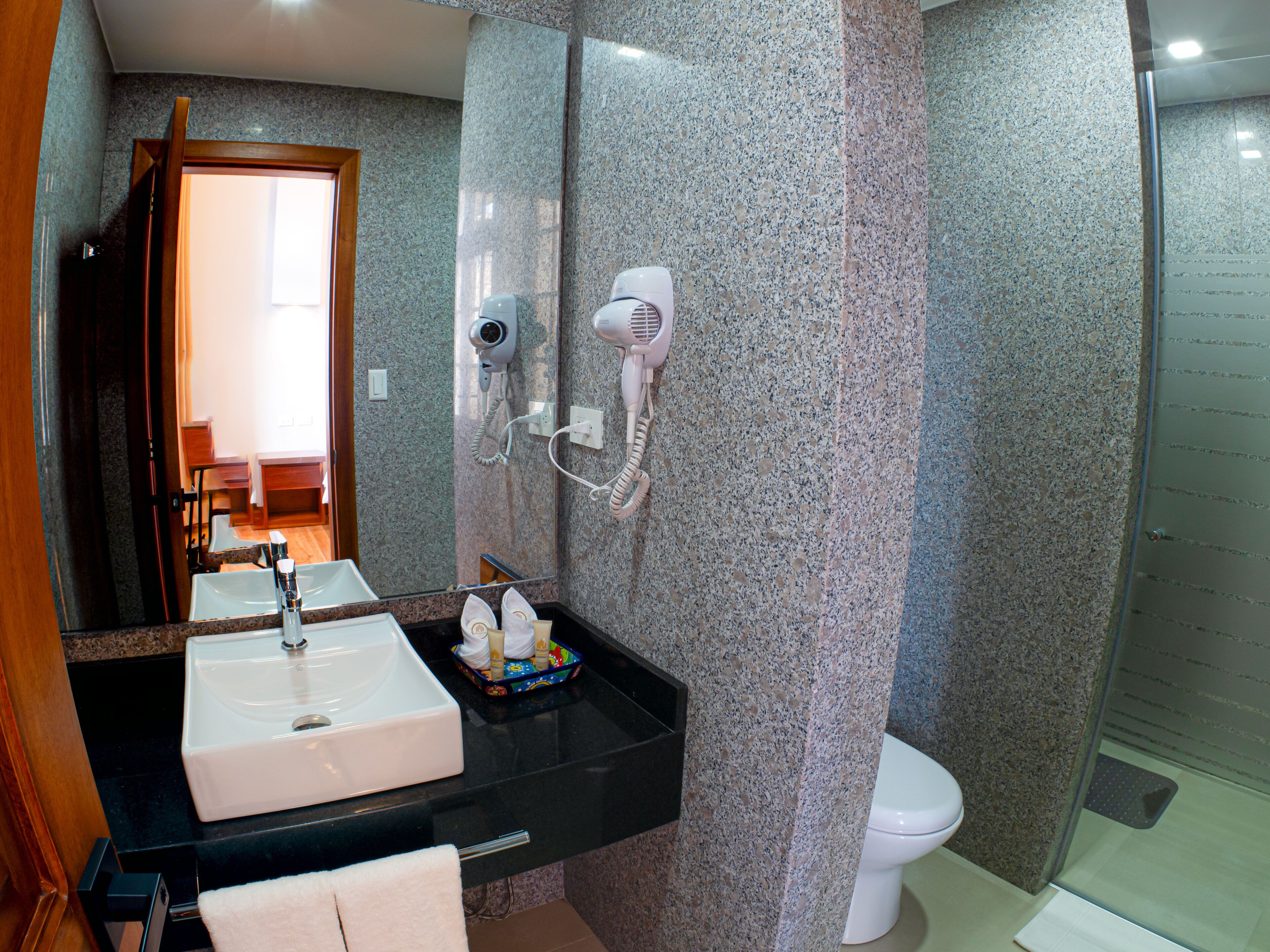 Casa de banho com bancada de granito, lavatório branco, secador de cabelo e sanita.