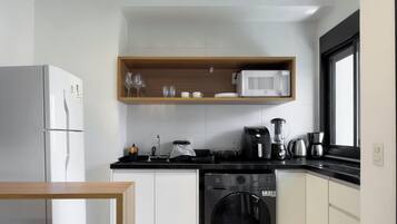 Uma cozinha compacta equipada com geladeira, micro-ondas, cafeteira e lava-louças.