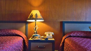 Quarto de hotel com duas camas, uma mesa de cabeceira com abajur, um telefone e um objeto decorativo.