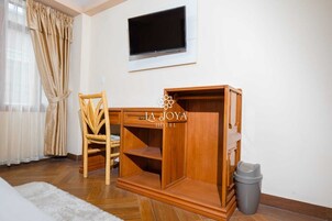 Quarto de hotel com um armário de madeira, uma televisão na parede, uma cadeira e um tapete branco.
