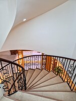 Escadaria espiral com grades ornamentadas pretas e degraus bege.