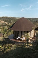 Um edifício circular com telhado cónico, rodeado por vegetação exuberante e colinas ao fundo.