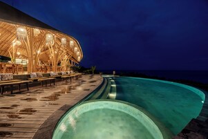 Área à beira da piscina com piscina em curva, deck de madeira e disposição de assentos.