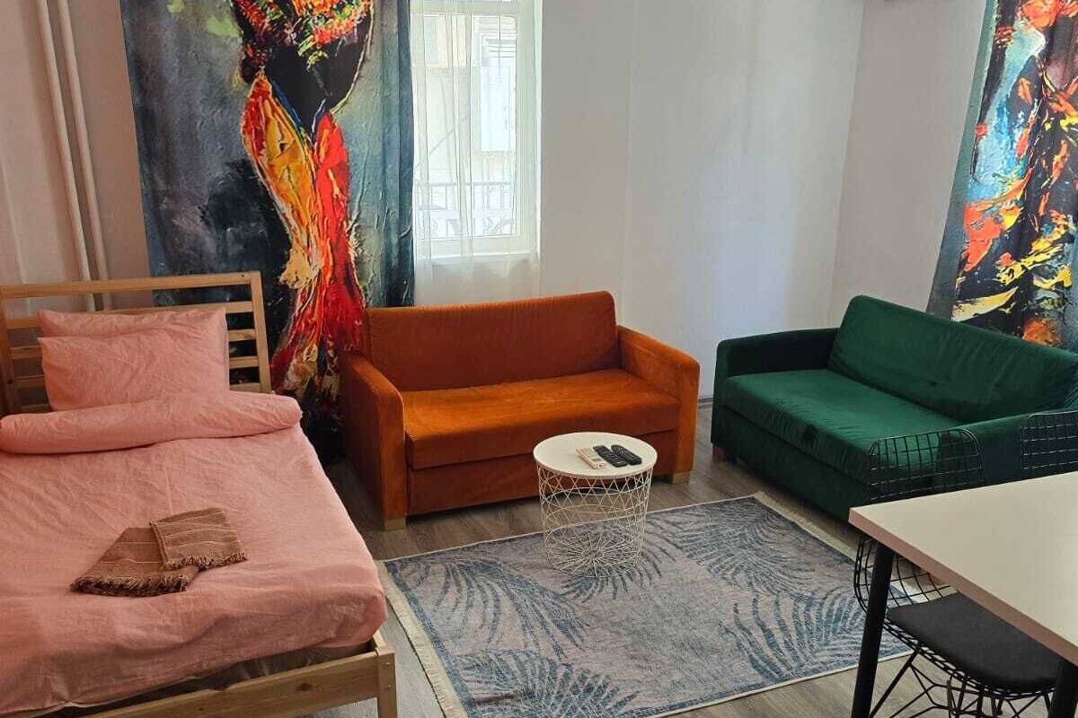 Quarto moderno e bem iluminado com cama, dois sofás, uma mesinha redonda e uma mesa de jantar.