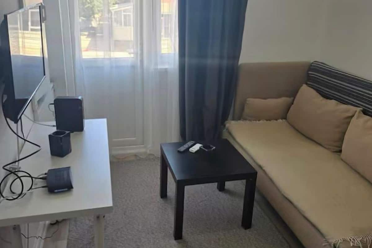 Uma sala de estar com sofá, mesinha, televisão e janela com cortinas.