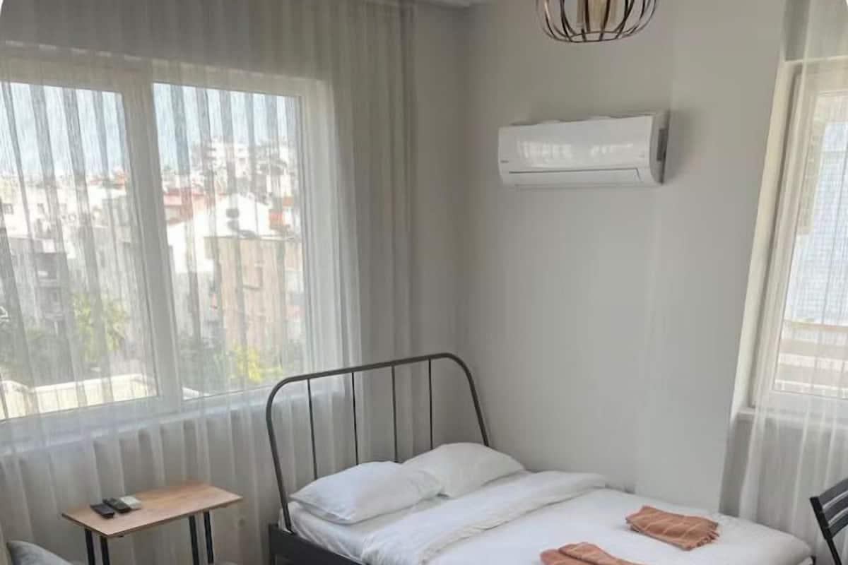 Quarto compacto com cama, uma mesinha e um sofá.