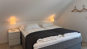 Quarto com cama, duas luminárias de cabeceira, mesa de cabeceira e cabideiro fixado na parede.