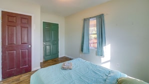 Um quarto com uma cama, uma porta vermelha, uma porta verde e uma janela com cortinas.