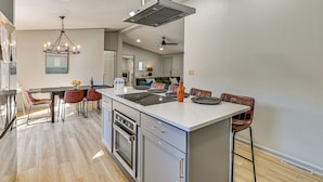 Cozinha moderna com ilha central, eletrodomésticos de aço inoxidável e área de jantar com cadeiras vermelhas.