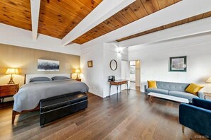 Quarto com cama, mesas de cabeceira, um banquinho, sofá e escrivaninha.