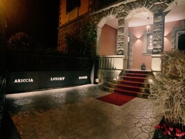 Entrada de uma casa luxuosa, com tapete vermelho e degraus de pedra.