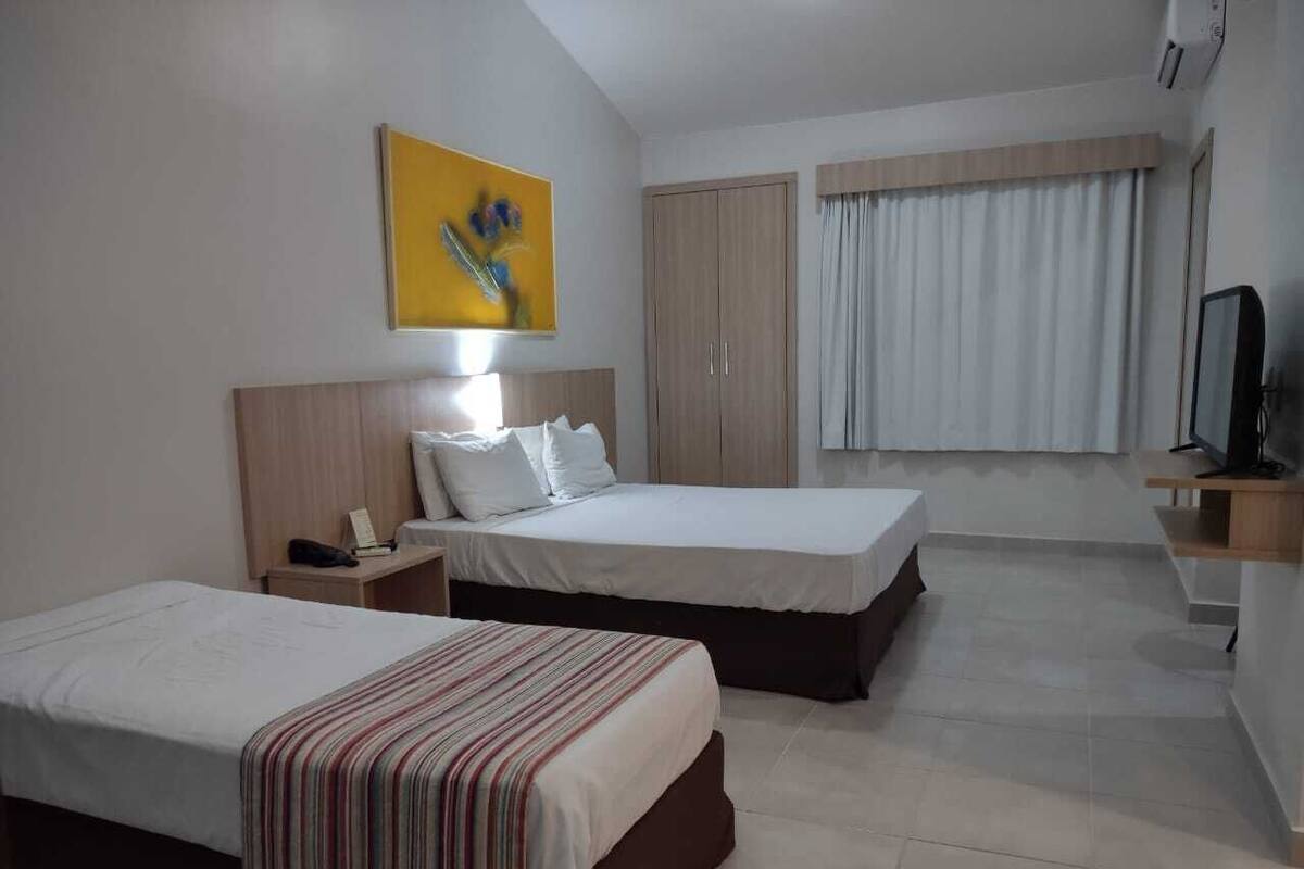 Quarto de hotel com duas camas, um guarda-roupa, uma televis ão e um quadro na parede.