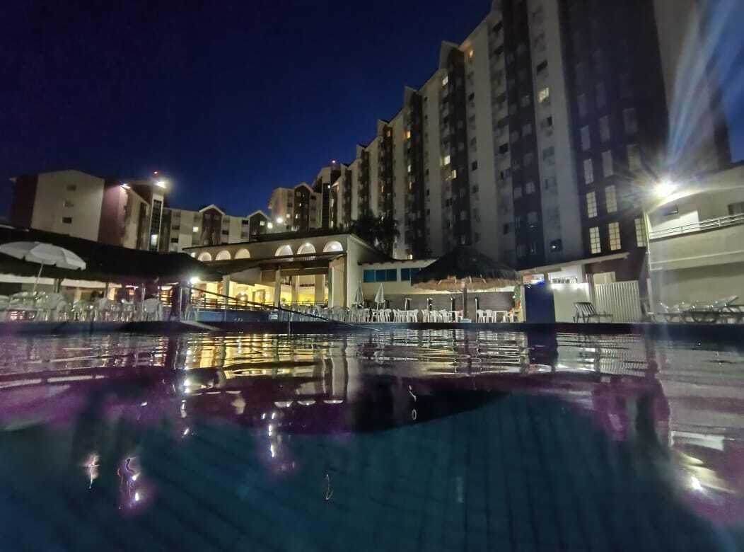 Vista noturna de um hotel com piscina refletindo luzes.