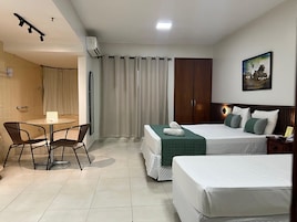 Quarto de hotel com cama, escrivaninha com cadeiras, guarda-roupa e um quadro na parede.