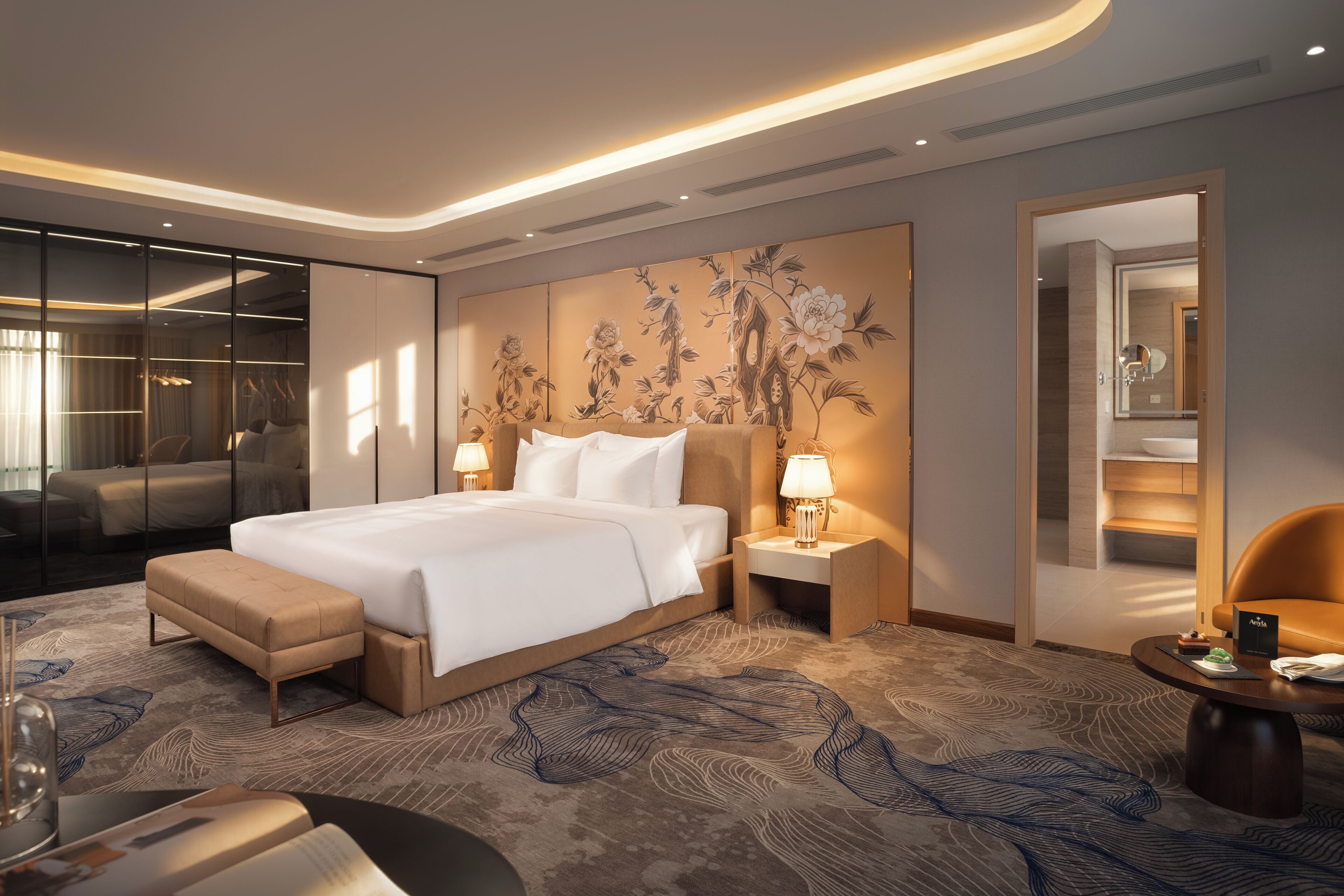 Quarto de hotel moderno com cama grande, mesas de cabeceira, área de estar e uma janela ampla.