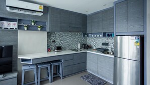 Uma cozinha moderna com armários cinza, bancada branca e geladeira de aço inoxidável.