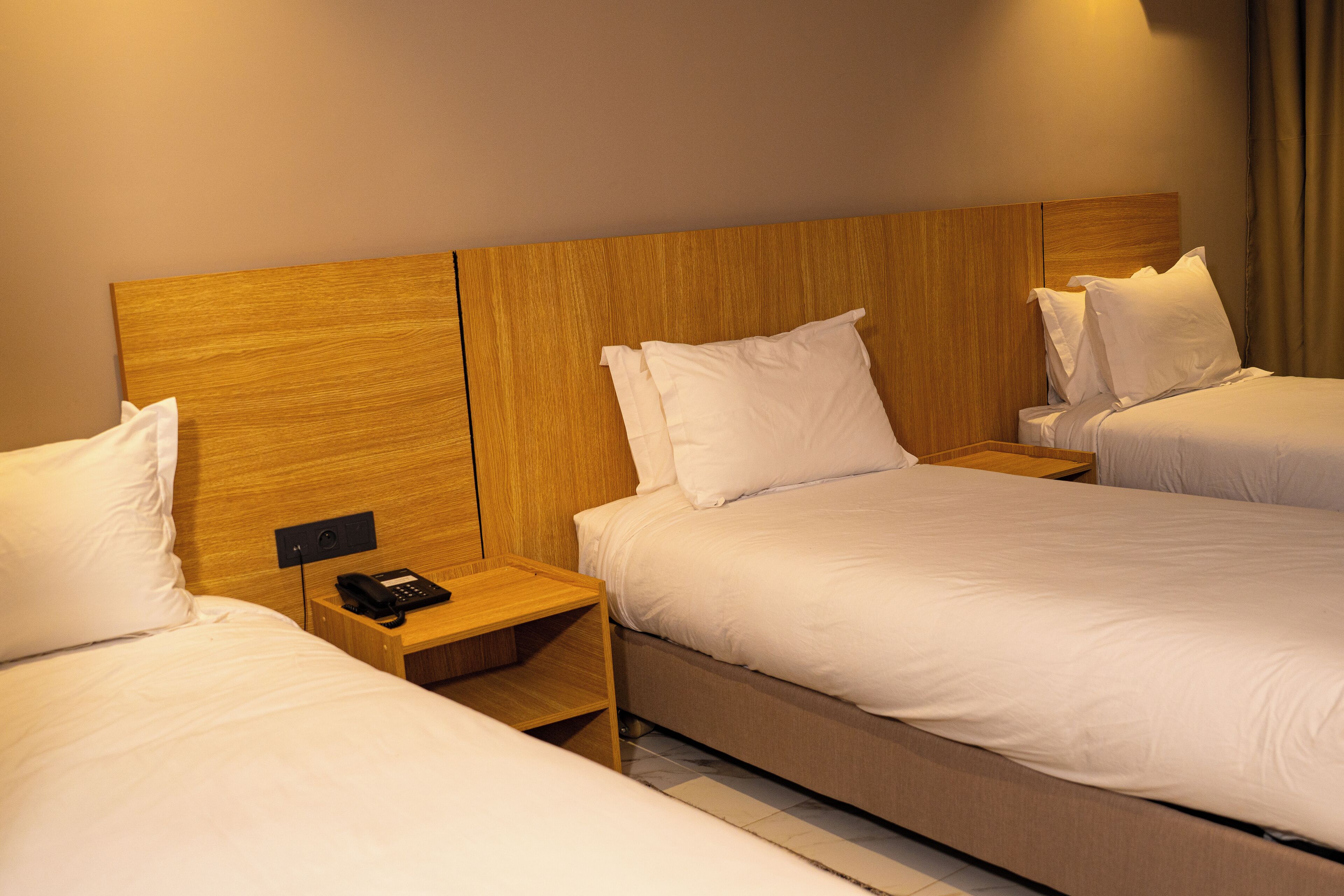 Quarto de hotel com duas camas de solteiro, cabeceiras de madeira, roupa de cama branca e mesa de cabeceira com telefone.