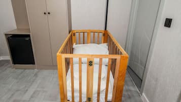 Um berço de madeira com rodinhas em um quarto com soalho de madeira clara, um guarda-roupa e uma porta.