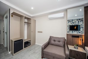 Quarto moderno com sofá, uma pequena mesa com uma planta, TV fixada na parede e prateleiras embutidas.