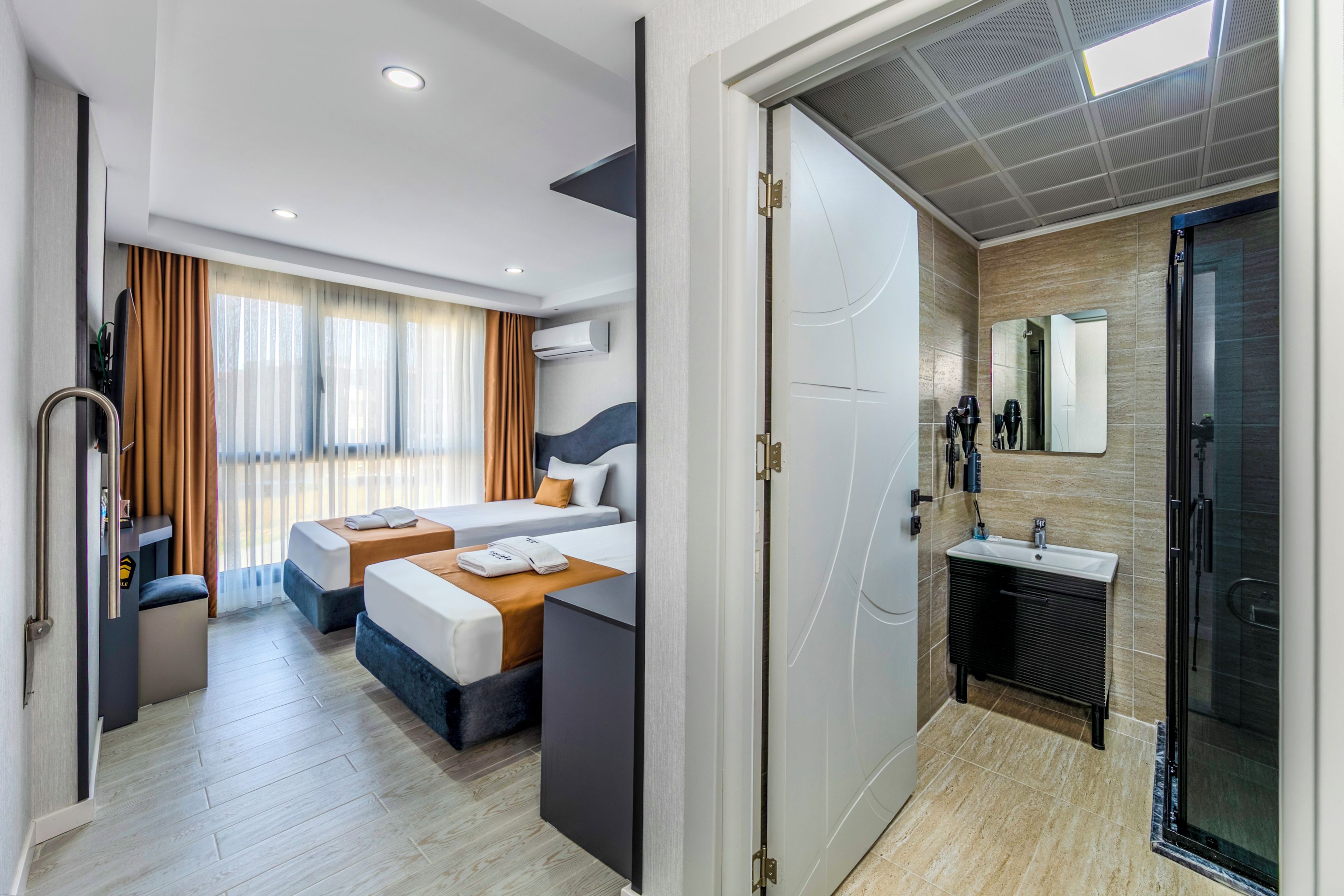 Quarto de hotel com duas camas, banheiro com pia e espelho, e vista para o exterior.