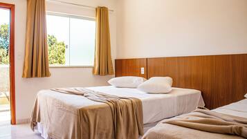 Quarto de hotel com duas camas, roupa de cama bege, cabeceira de madeira e uma janela com cortinas.