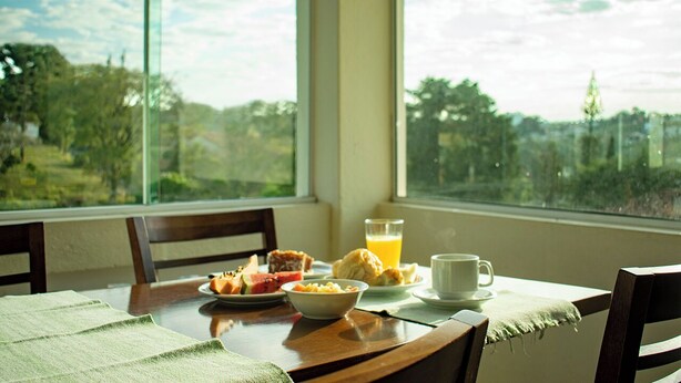 Mesa de café da manhã com vista para uma paisagem verde através de janelas amplas.