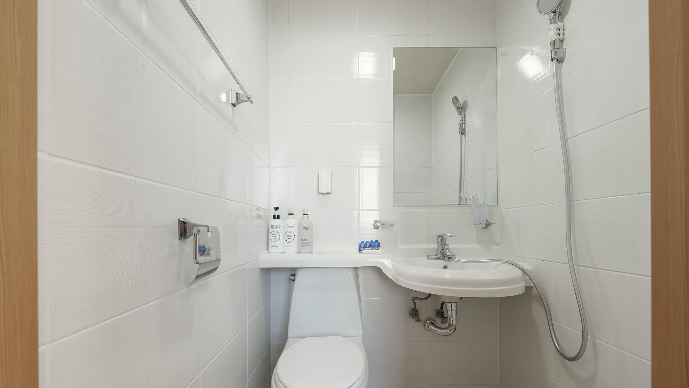 Um banheiro pequeno e moderno com azulejos brancos, vaso sanitário, pia e chuveiro.