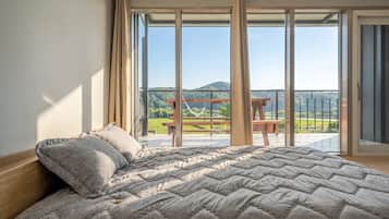 Quarto com uma cama grande, vista para uma varanda com mesa de madeira e paisagem panorâmica.