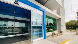Um edifício moderno com entrada de vidro, parede azul e área verde com plantas.