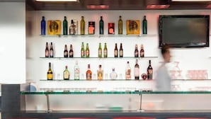 Uma área de bar com prateleiras cheias de garrafas de bebidas, uma televisão de tela plana e banquetas vermelhas.