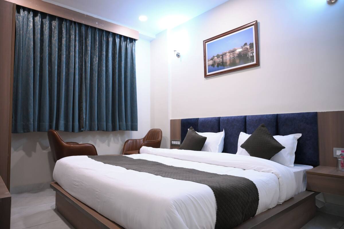 Quarto de hotel moderno com uma cama grande, cabeceira, uma cadeira, mesa de cabeceira e um quadro na parede.