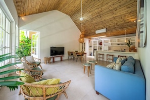 Uma sala de estar ampla com teto alto, televisão, mesa de jantar e cozinha.