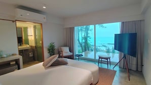Quarto de hotel com uma cama grande, uma televisão em suporte, uma mesa pequena e vista para o mar.