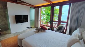 Quarto de hotel moderno com uma cama grande, televisão na parede, varanda com vista para o mar e uma pequena mesa com uma cadeira.
