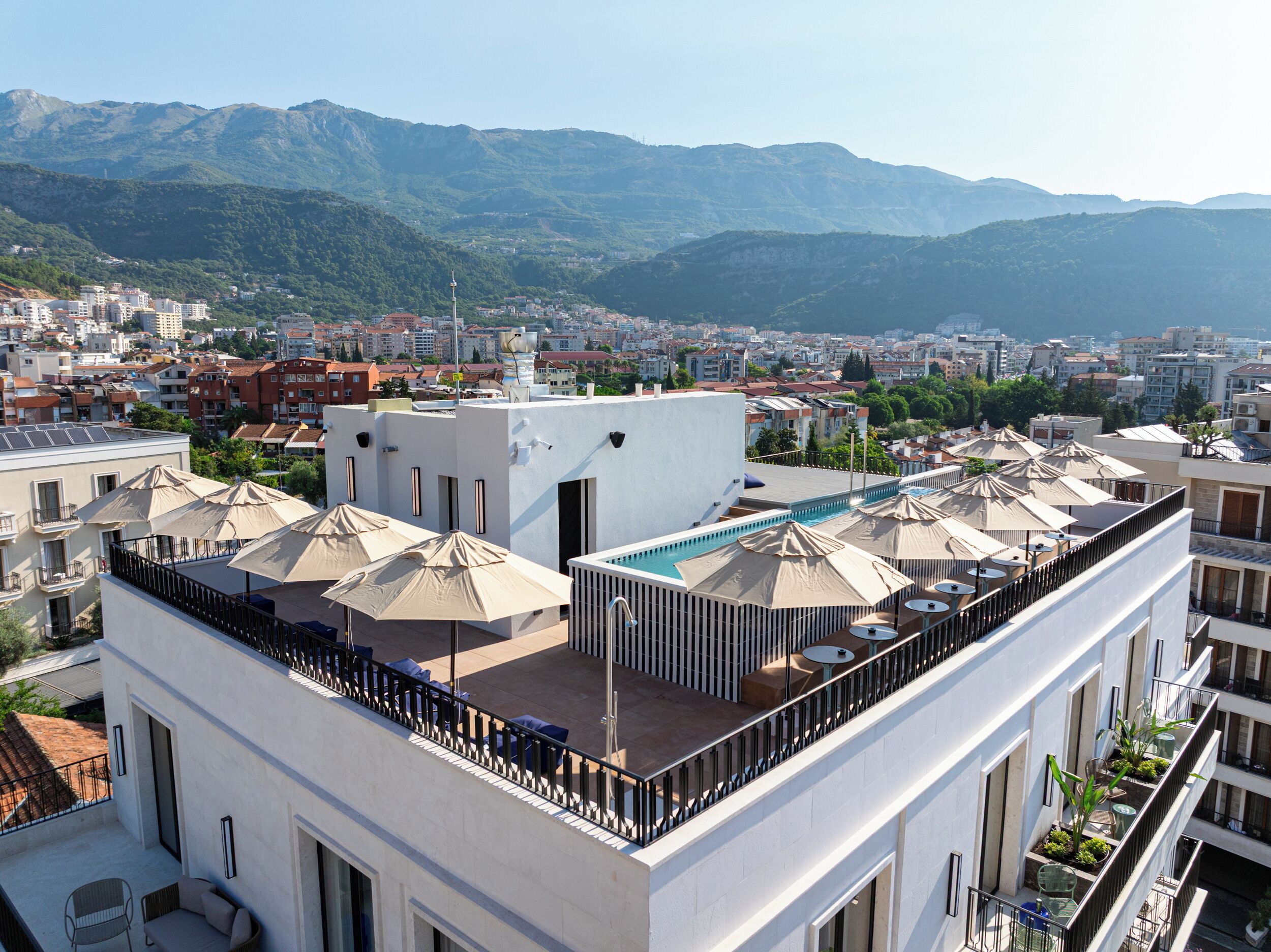 Terraço no telhado com área de estar externa e piscina, com vista para a paisagem urbana e montanhas.