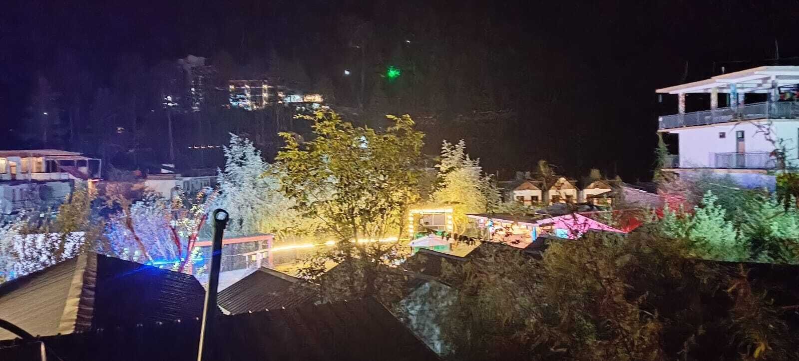 Vista noturna de um bairro residencial com edifícios e árvores iluminados.