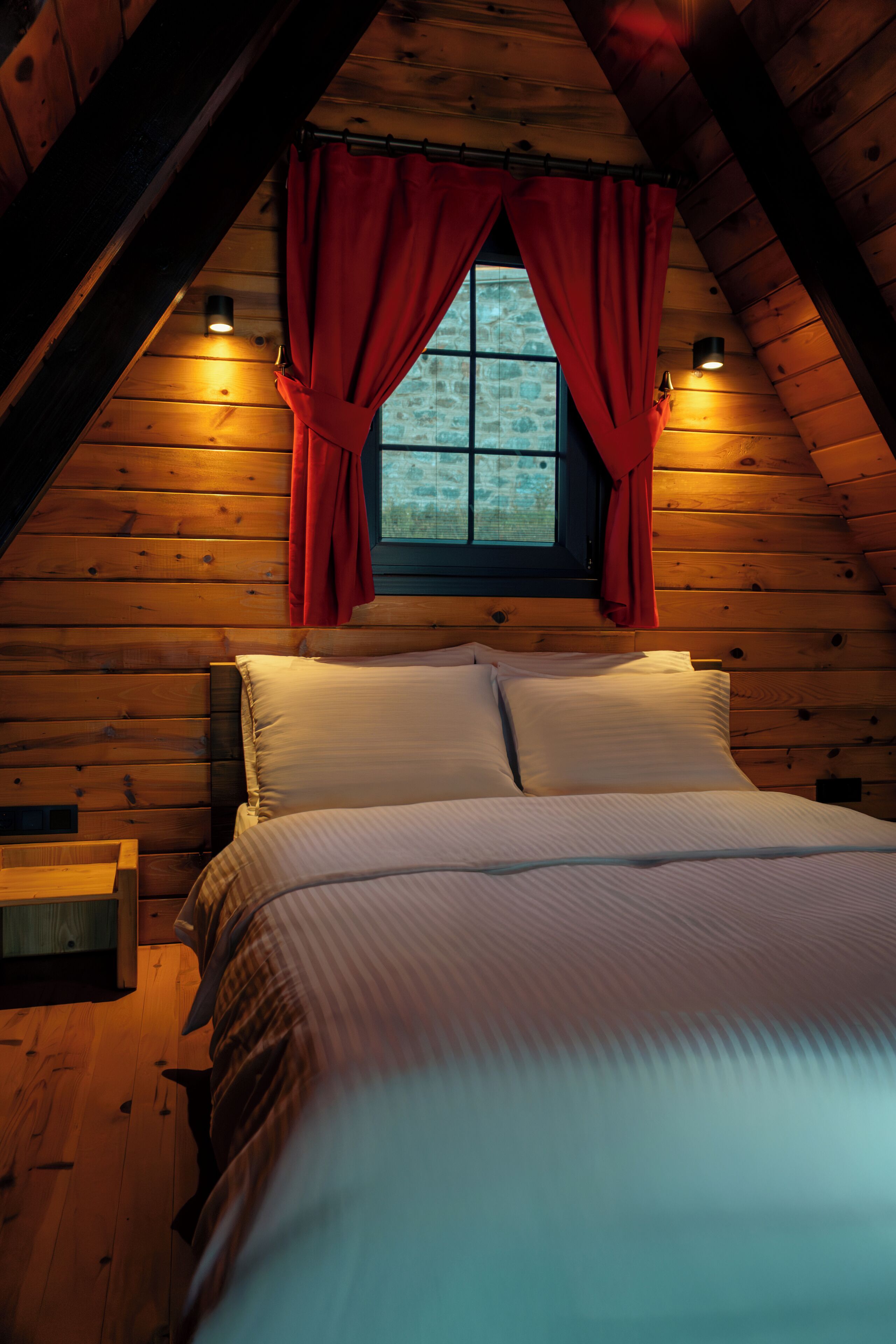 Quarto de cabana de madeira aconchegante, com cama, cortinas vermelhas e janela.