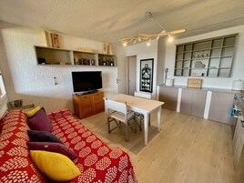 Um espaço compacto com sofá, televisão, mesa de jantar e uma kitchenette.