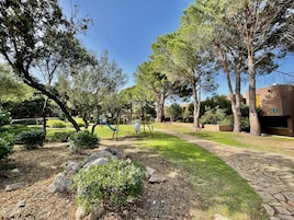 Um parque com brinquedos, árvores e um caminho de pedra.