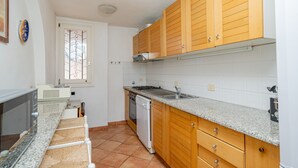 Cozinha com armários de madeira, bancada de granito, lava-louças e janela com grades decorativas de ferro.